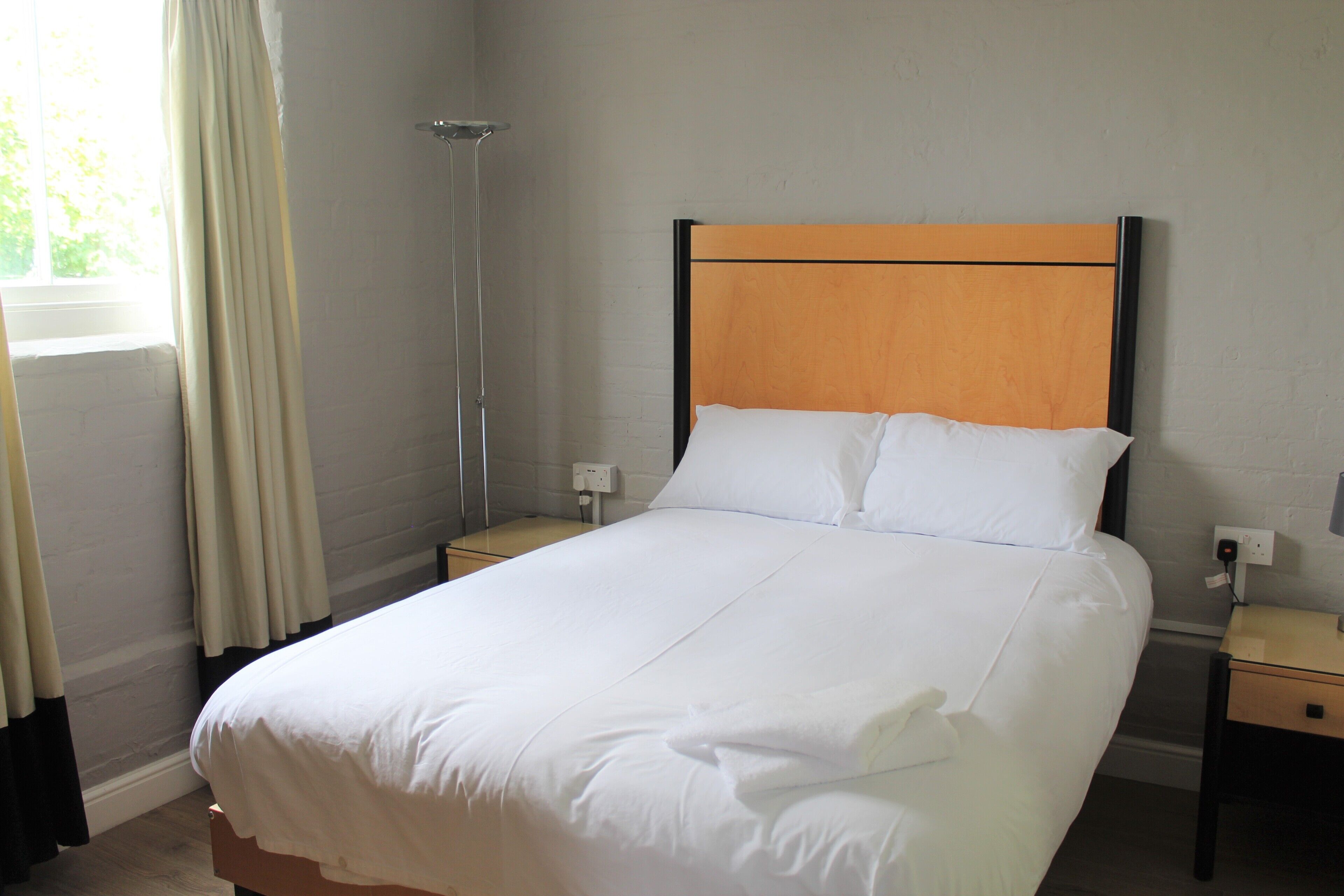 Uma cama bem arrumada com lençóis brancos em um quarto com cabeceira de madeira, mesa de cabeceira e abajur.