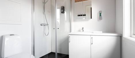 Uma casa de banho moderna com cabine de chuveiro em vidro, sanita branca e toucador branco com espelho.