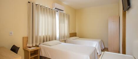 Quarto de hotel com duas camas, uma escrivaninha, uma cadeira, ar condicionado, televisão e guarda-roupa.