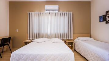 Quarto de hotel com uma cama grande, duas mesas de cabeceira, uma escrivaninha e um ar condicionado.