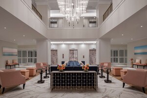 Um hall amplo com área de estar central, um candelabro e vista para o andar superior.