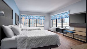 Quarto de hotel moderno com duas camas, televisão e janelas amplas com cortinas estampadas.