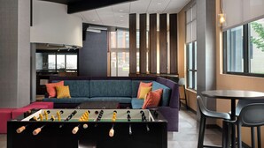 Uma área de estar moderna com sofá, mesa de pebolim e um bar com banquetas.