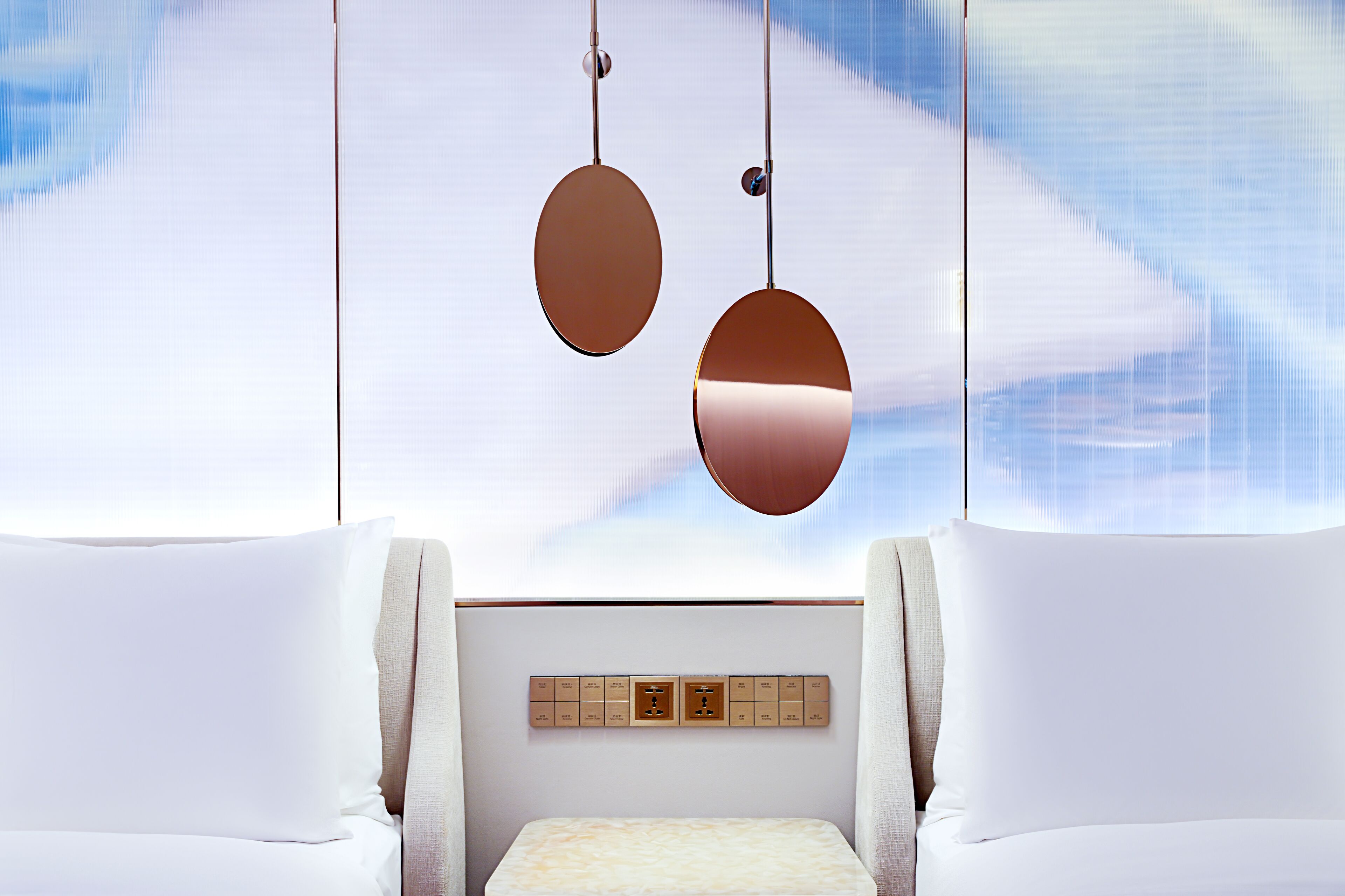 Quarto de hotel moderno com uma janela grande, dois espelhos esféricos pendurados e uma mesa de cabeceira com abajur.