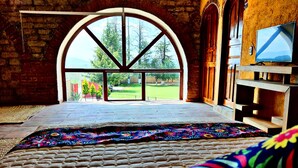 Um quarto com uma grande janela em arco, uma cama com colcha estampada e uma televisão sobre um suporte de madeira.