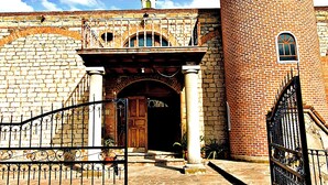Um edifício histórico com uma grande torre de tijolos, uma entrada em arco e um pátio murado.