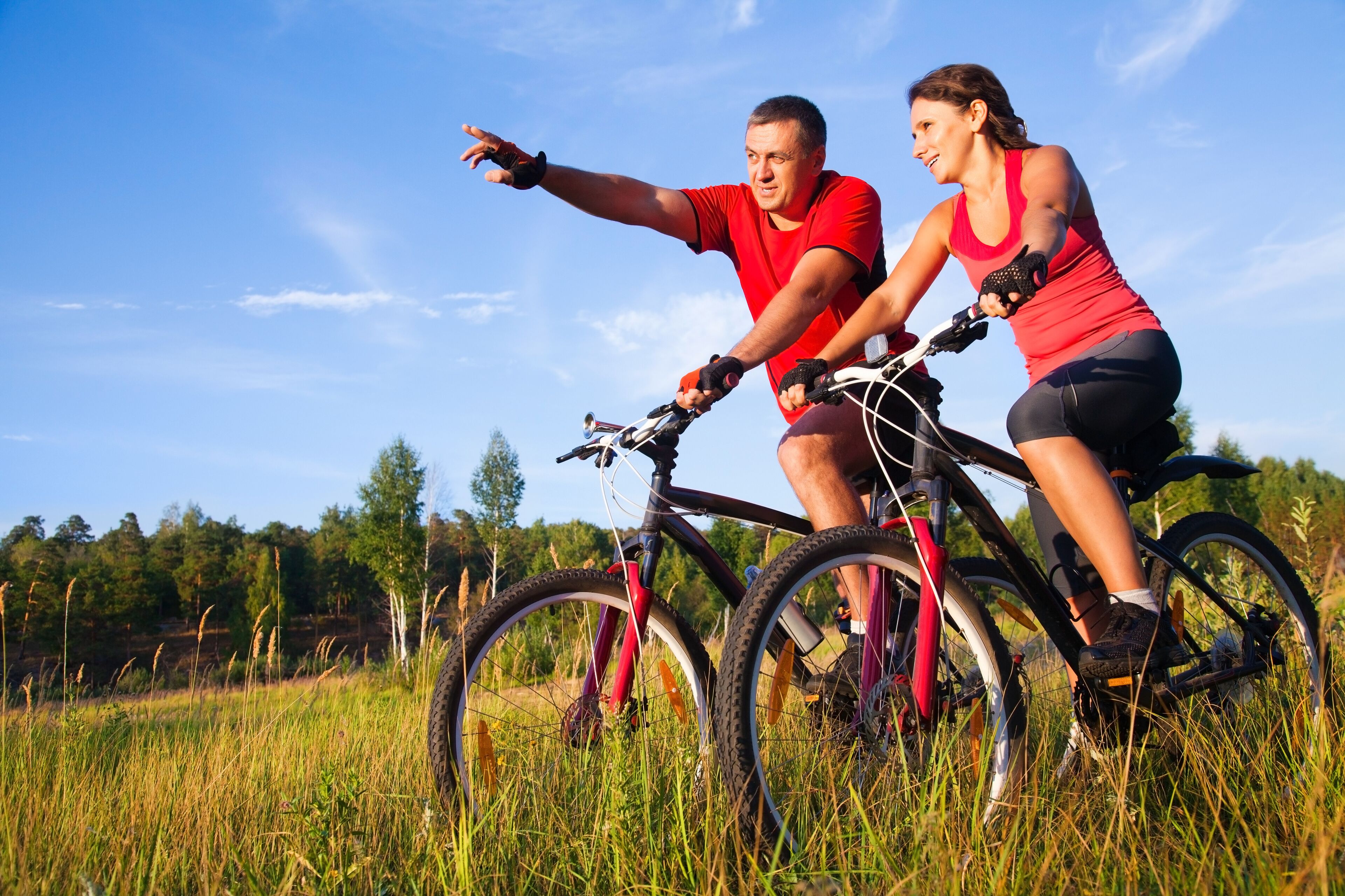 Duas pessoas em bicicleta de montanha em um campo gramado, com árvores ao fundo.