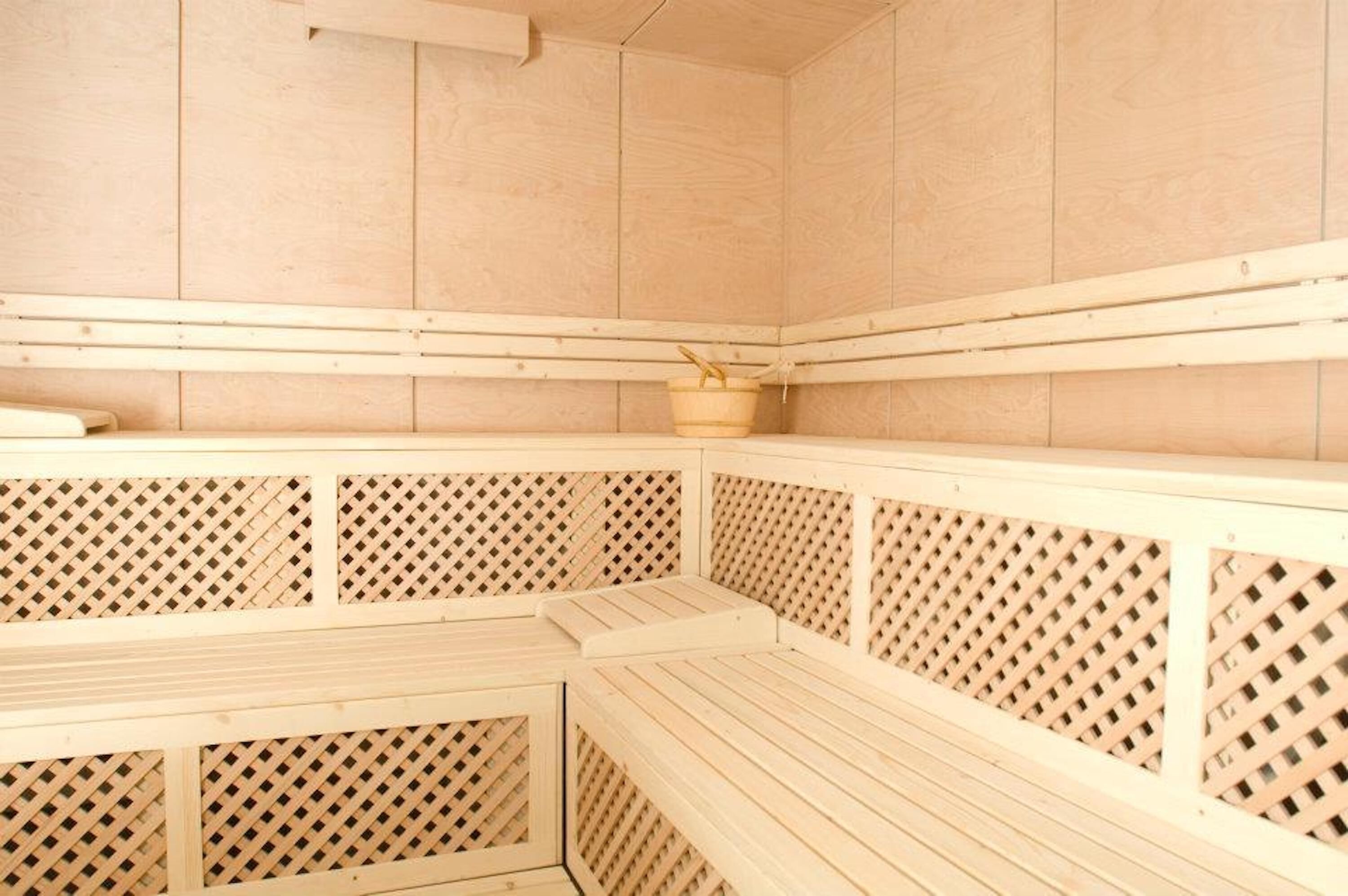Uma sauna de madeira com design treliçado, bancos e um balde de madeira com concha.