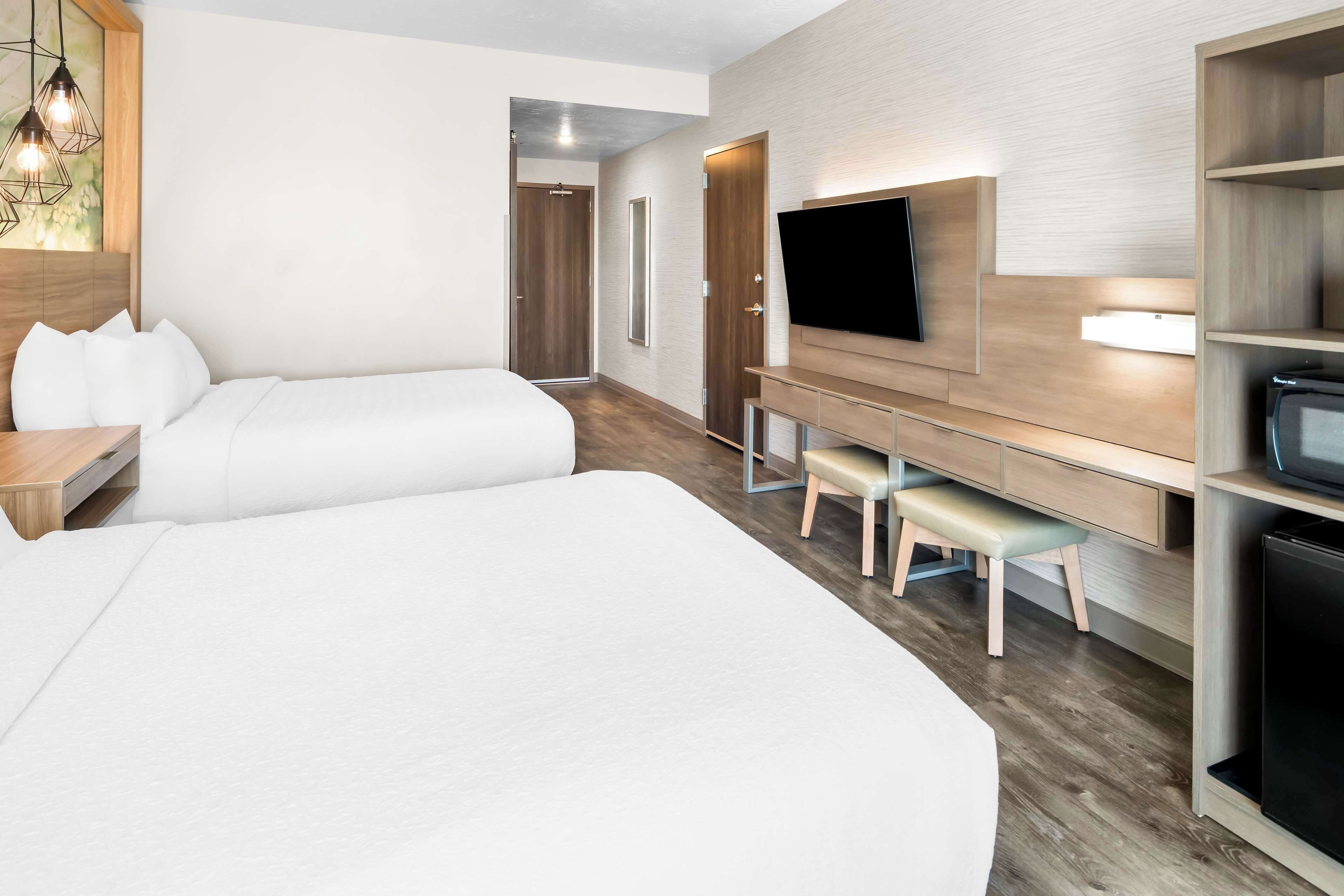 Quarto de hotel com uma cama grande, uma escrivaninha com cadeira, televisão e estante de livros.