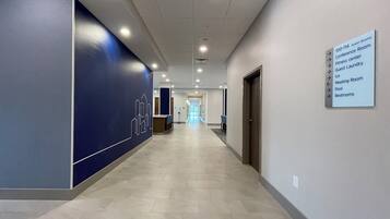 Corredor de hotel com aviso listando comodidades como quartos de hóspedes, sala de conferências, centro de atividades físicas, lavanderia para hóspedes, máquina de gelo, sala de reuniões, piscina e sanitários.