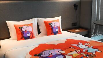 Quarto de hotel com cama, duas almofadas com personagens de desenho animado, mesa de cabeceira e criadeira.
