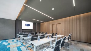 Uma sala de conferências com uma tela grande, várias mesas e cadeiras.
