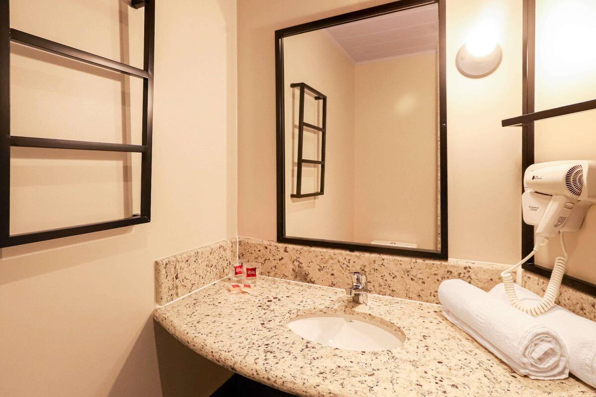 Uma casa de banho com bancada de granito, lavatório, espelho, secador de cabelo e toalha.