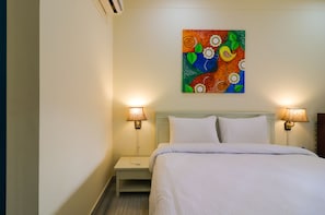 Quarto de hotel com uma cama, duas luminárias de cabeceira e um quadro abstrato colorido na parede.