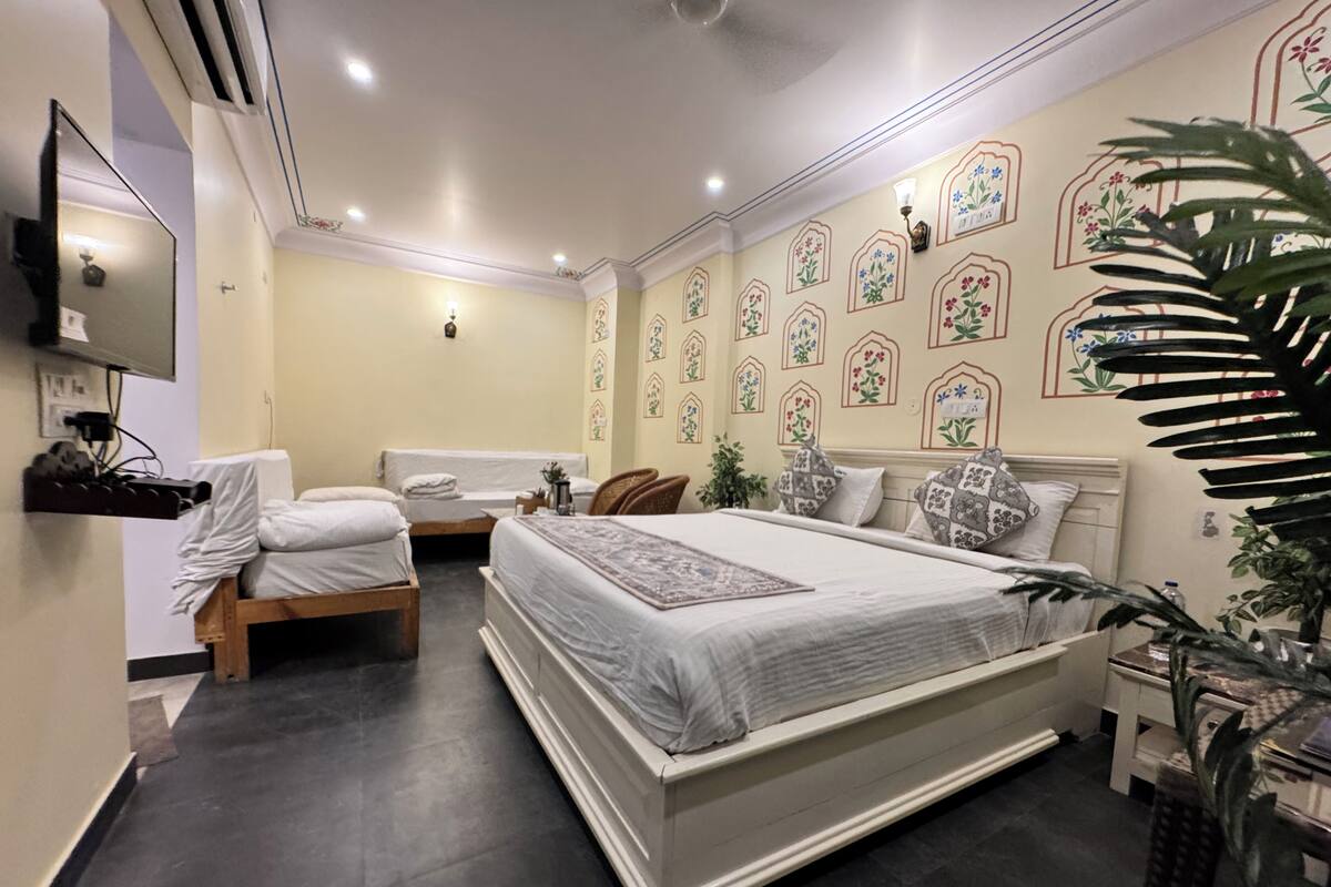 Quarto com uma cama grande, duas camas menores, uma televisão e padrões decorativos nas paredes.