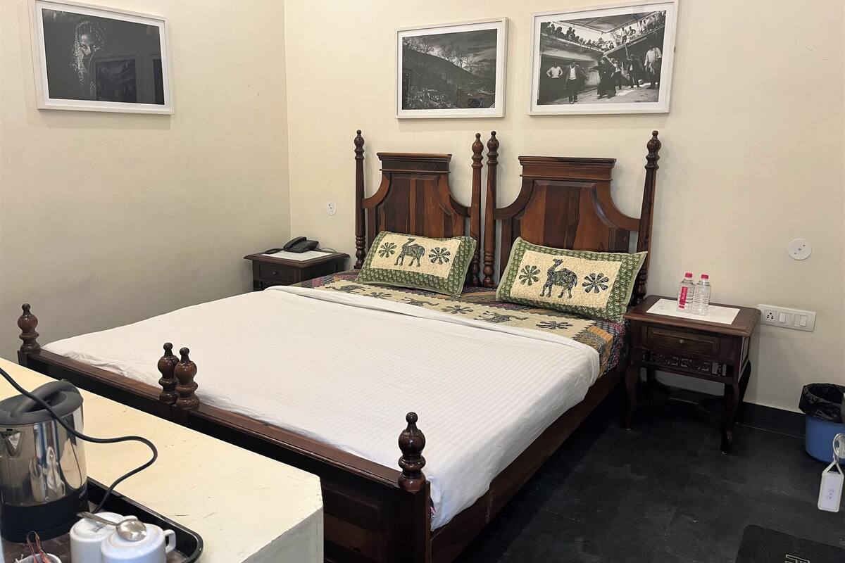 Uma cama bem arrumada com cabeceira de madeira, duas mesas de cabeceira com abajures e quadros nas paredes.