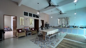 Ampla sala de estar com mesa de jantar, cadeiras, sofá, cozinha e ventilador de teto.