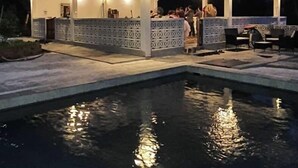 Uma área de estar coberta ao ar livre com uma piscina em primeiro plano.