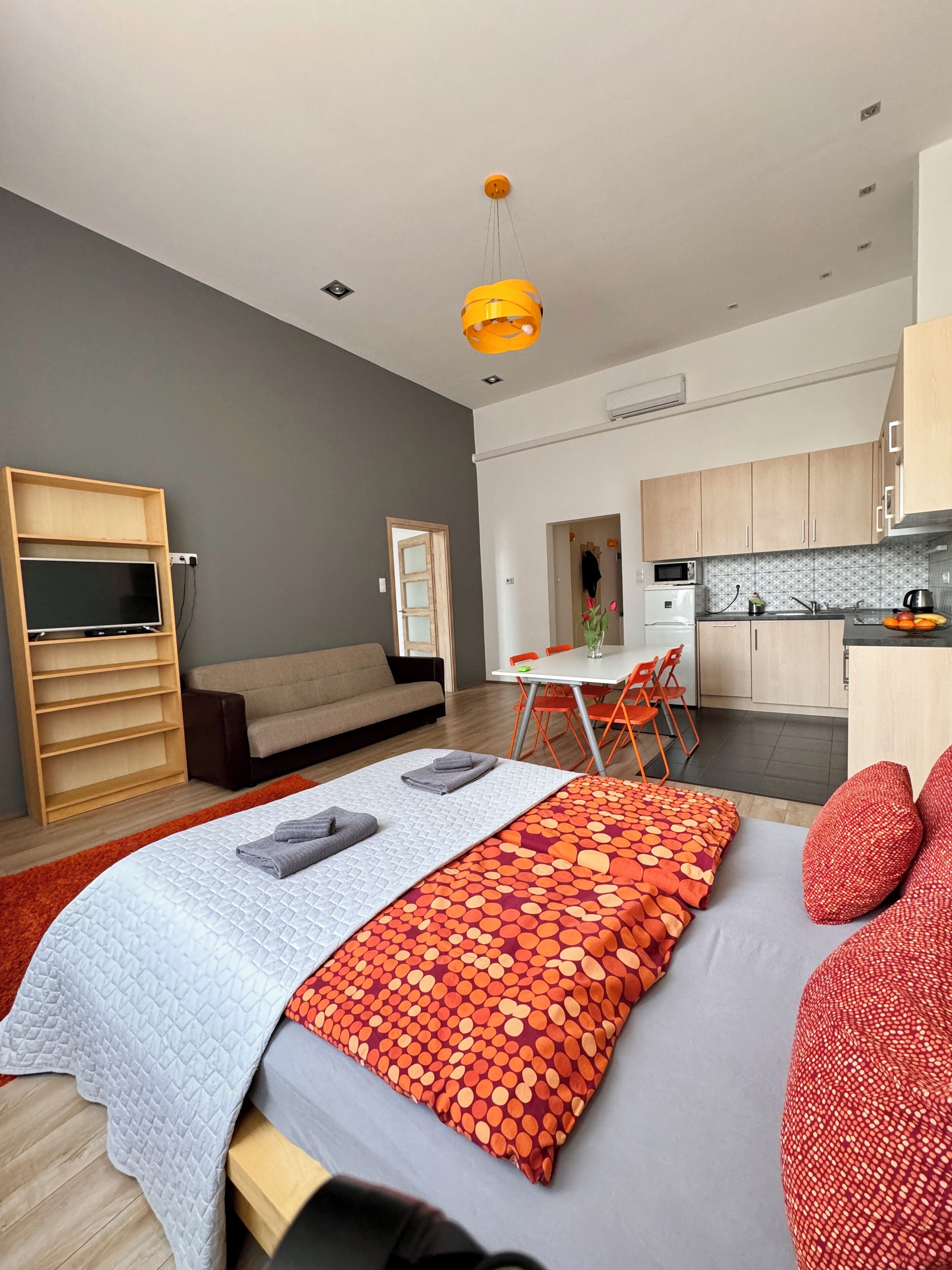 Quarto moderno com uma cama grande, um guarda-roupa de madeira, um sofá cinzento e um espaço de refeições com mesa e cadeiras.