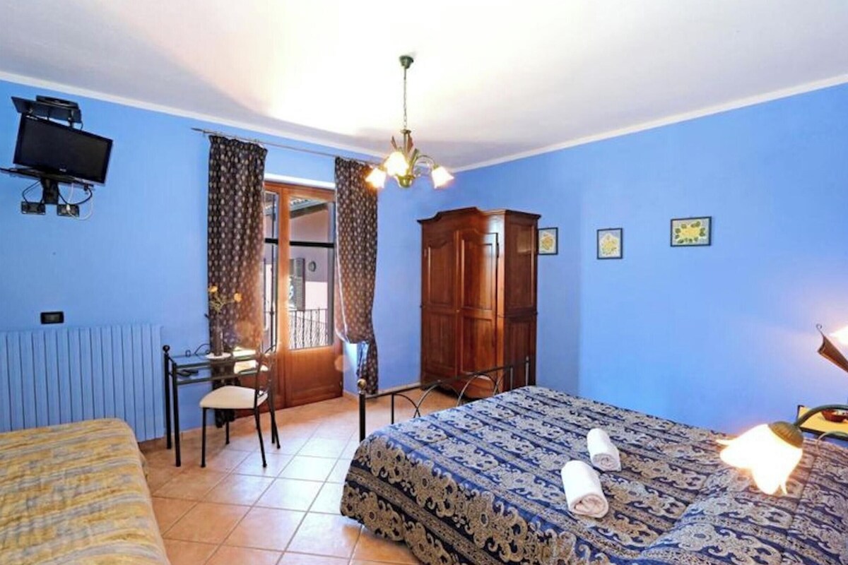 Quarto com uma cama, escrivaninha, cadeira, guarda-roupa e televisão.