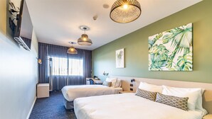 Quarto de hotel com duas camas, uma escrivaninha, uma cadeira e uma grande planta tropical na parede.