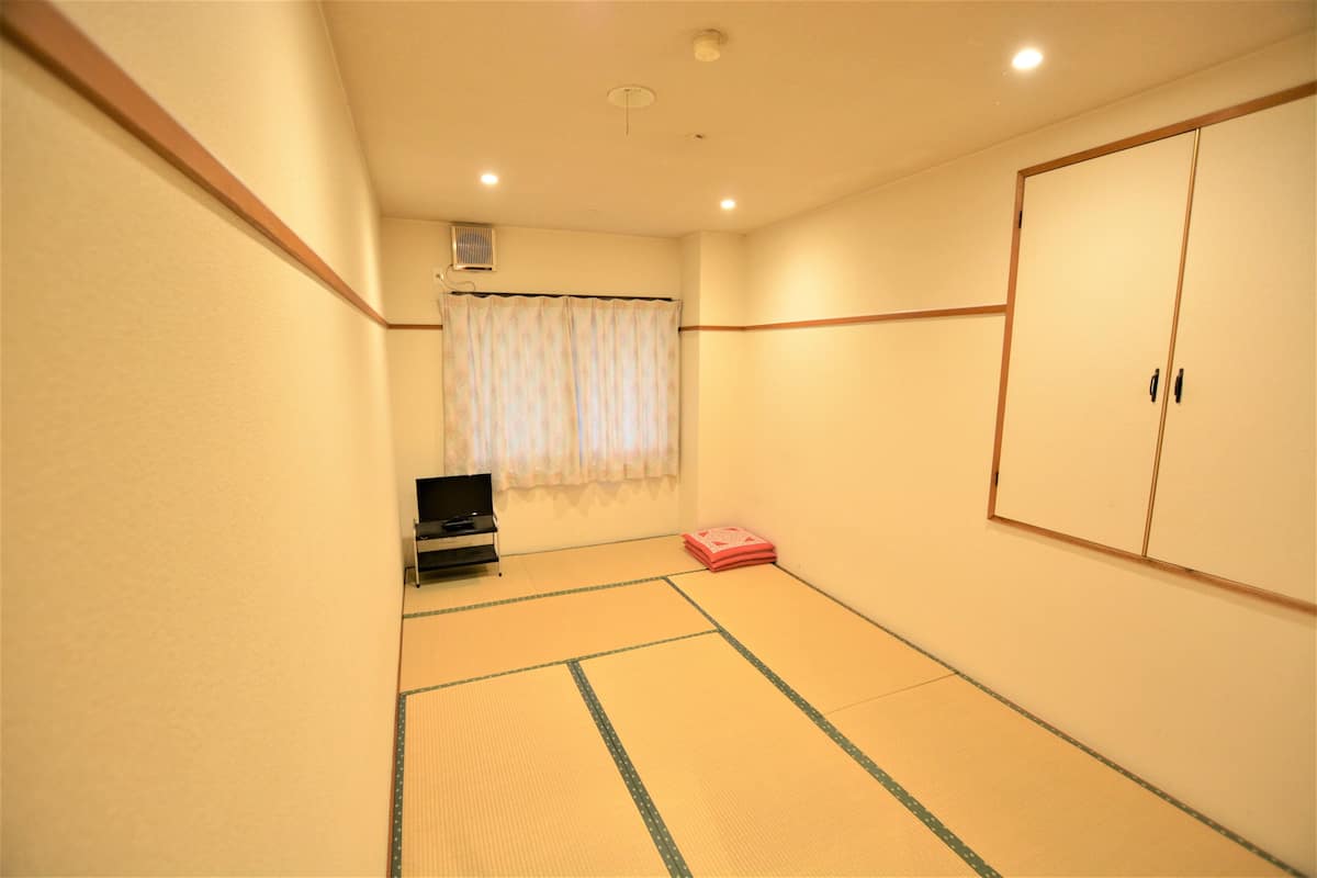 Quarto com piso de tatame, televisão, guarda-roupa e janela com cortina.