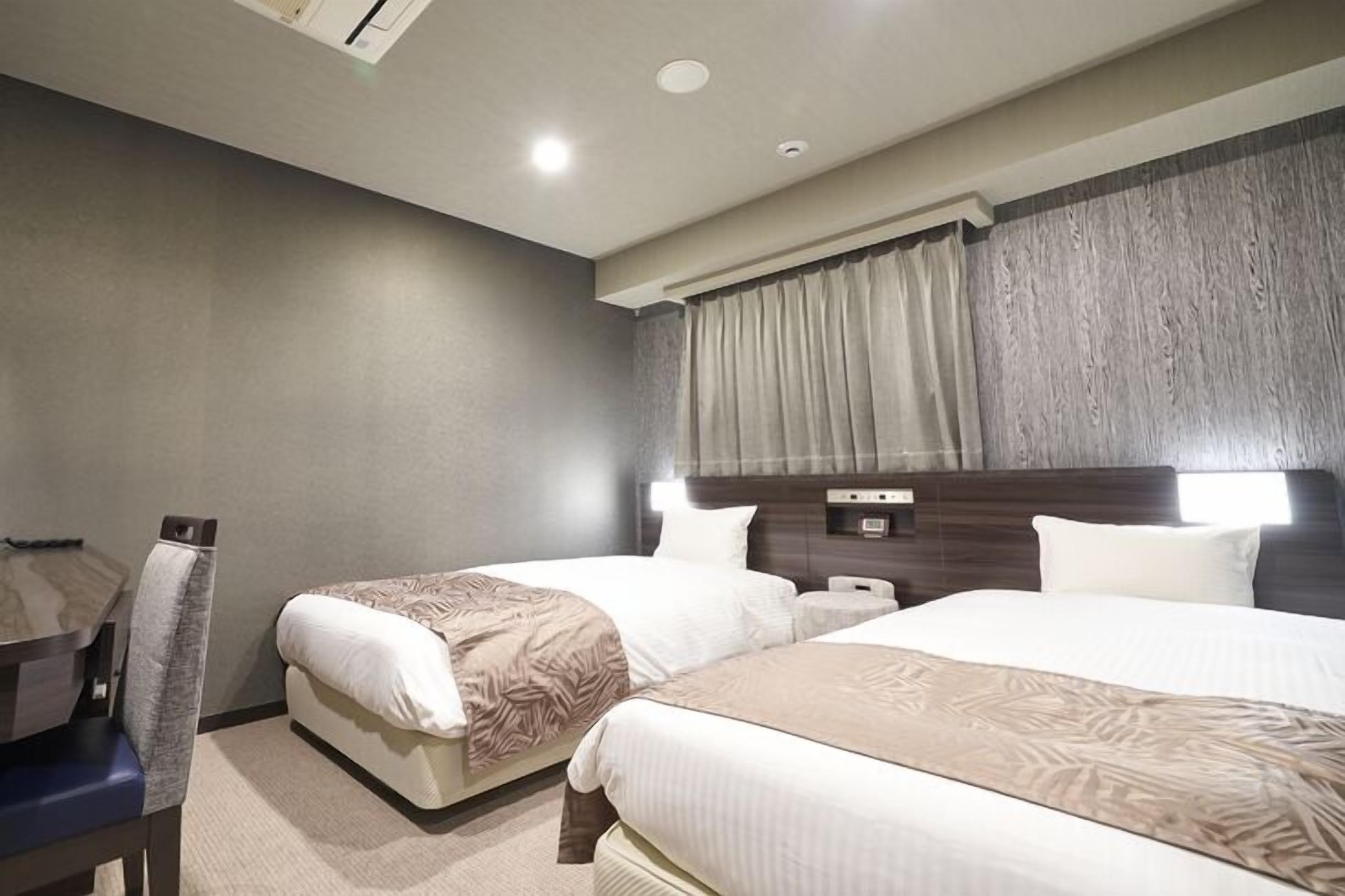 Quarto de hotel com duas camas, uma escrivaninha e uma cadeira.