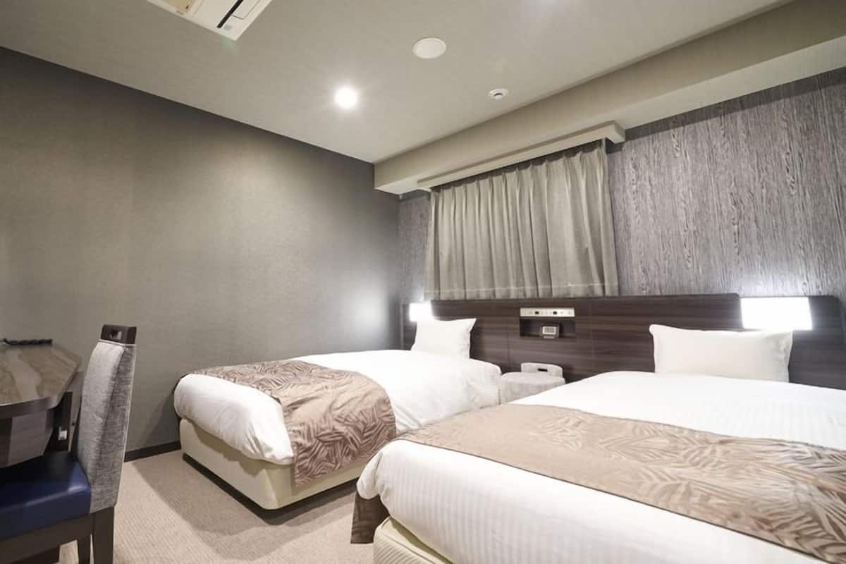 Quarto de hotel com duas camas, uma escrivaninha e uma cadeira.