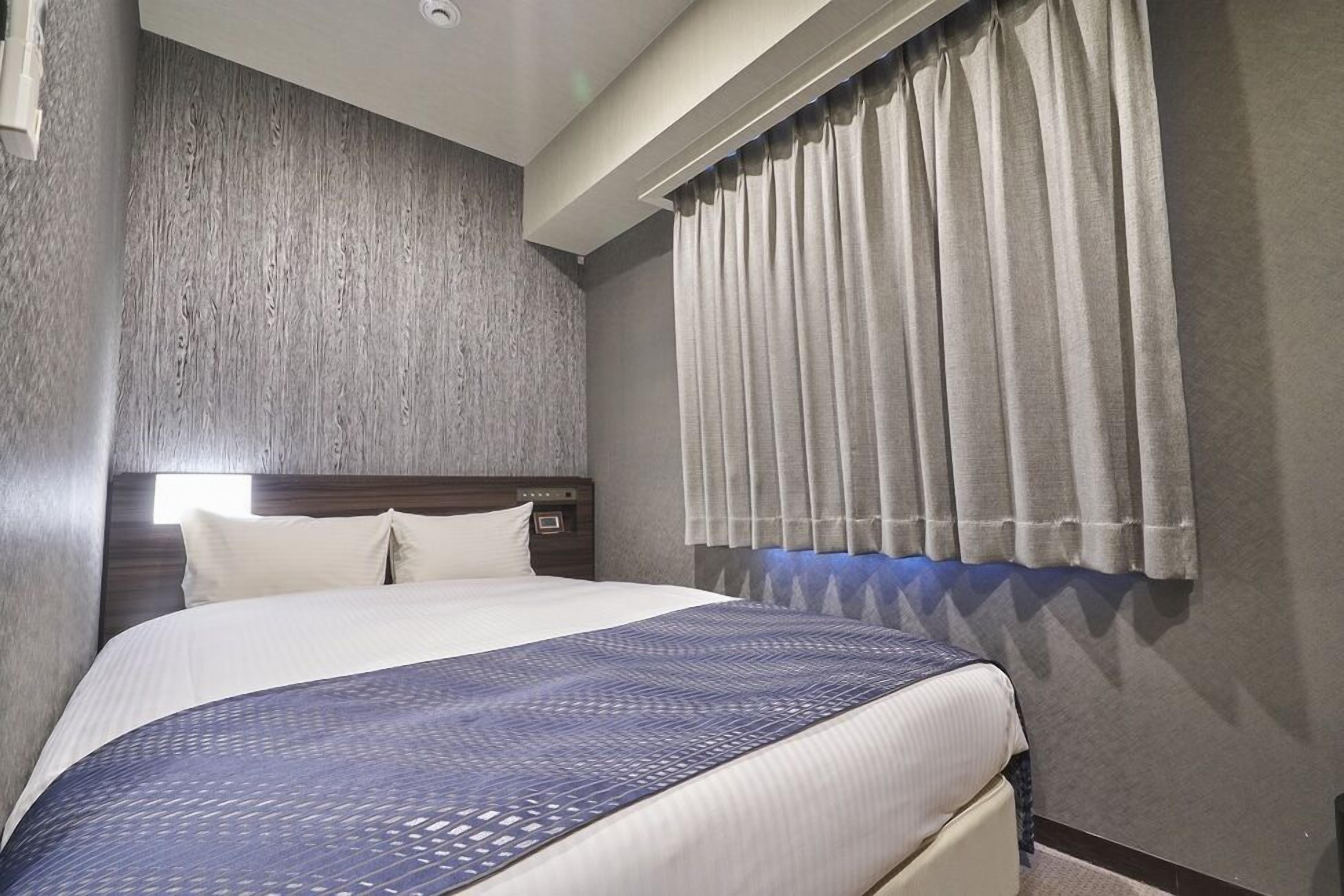 Quarto de hotel com uma cama grande, cabeceira, janela com cortinas e parede texturizada.