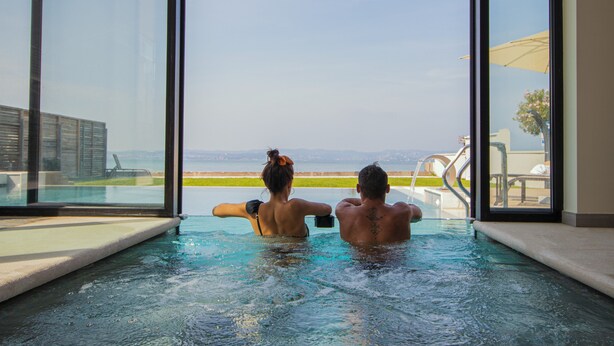 Um casal em banheira de hidromassagem privativa, com vista para a praia e oceano.