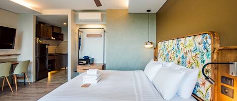 Quarto de hotel com cama, escrivaninha, cadeira, ventilador de teto e televisão.