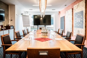 Uma sala de conferência com uma mesa comprida, cadeiras, uma televisão e um quadro branco.