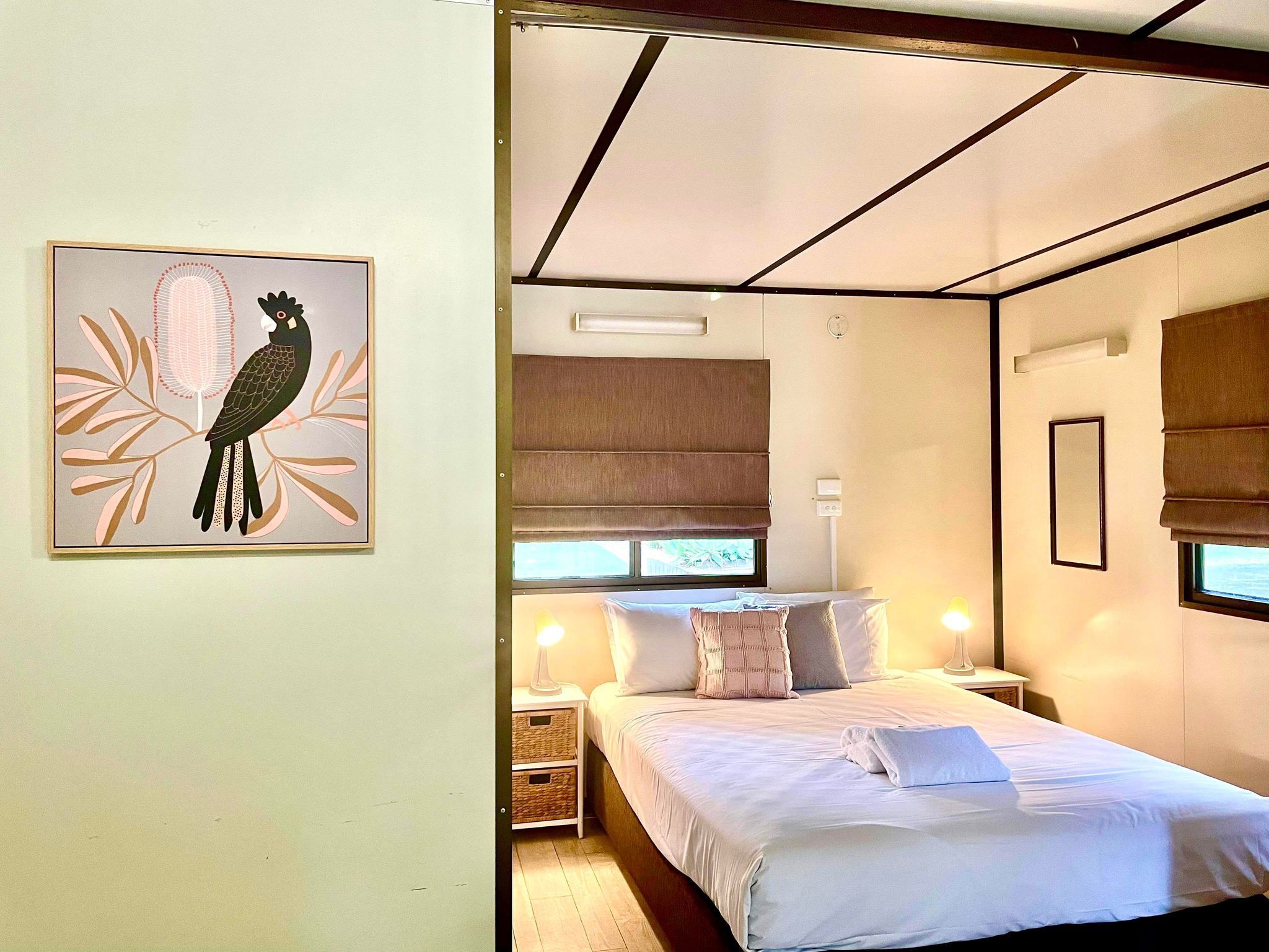 Quarto moderno com cama, mesas de cabeceira, um criado-mudo, janela com vista e uma obra de arte emoldurada na parede.