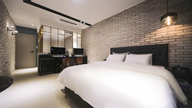 Quarto moderno com uma cama grande, uma escrivaninha com dois monitores e uma parede de tijolos.