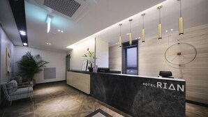 Uma área de recepção de hotel com balcão de mármore, iluminação pendente e um vaso de planta.