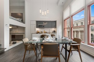 Uma área de refeições moderna com mesa de vidro, quatro cadeiras e cozinha ao fundo.