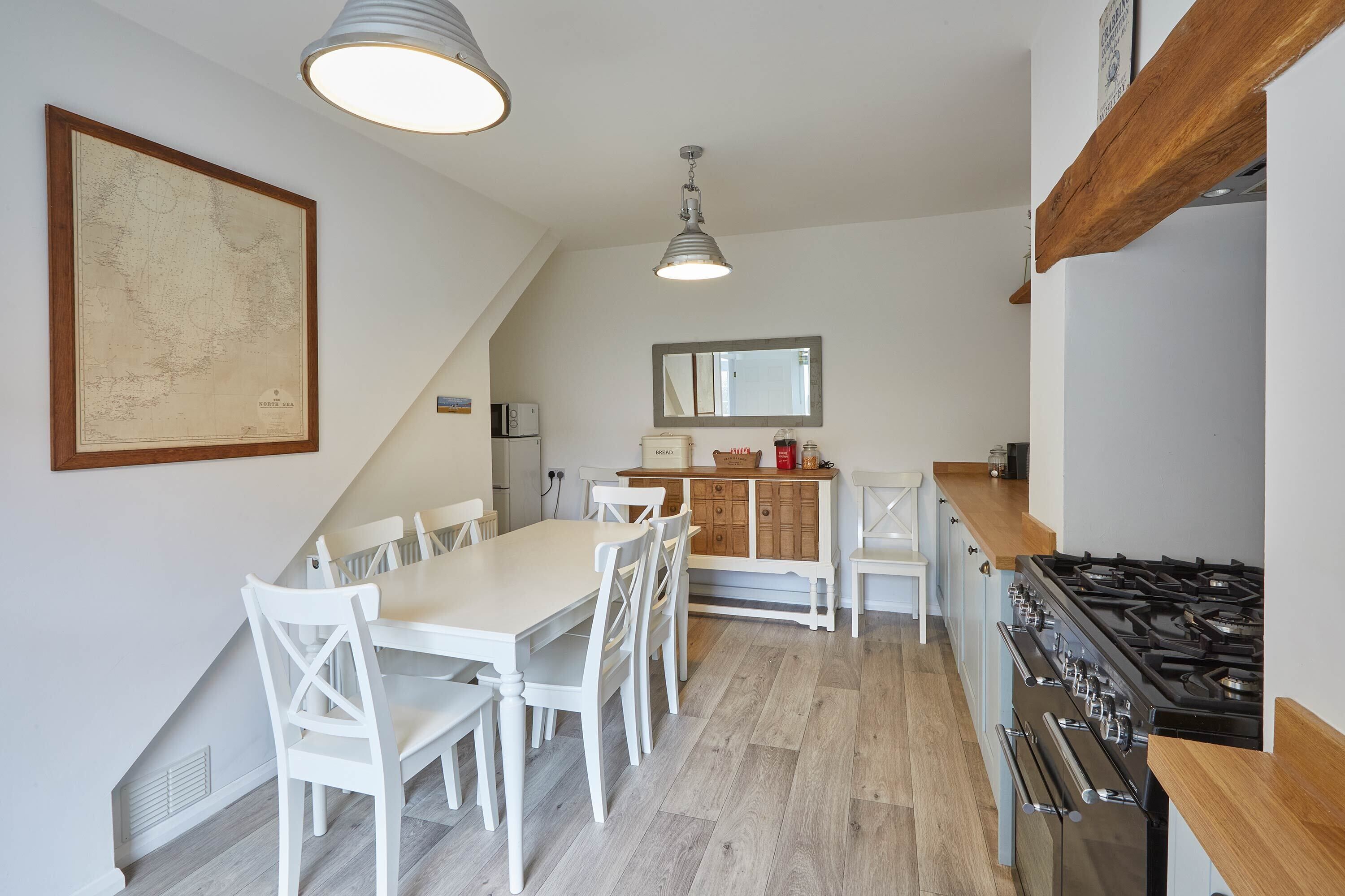 Uma cozinha com armários brancos, uma mesa de jantar com cadeiras, um fogão e uma luminária pendente.