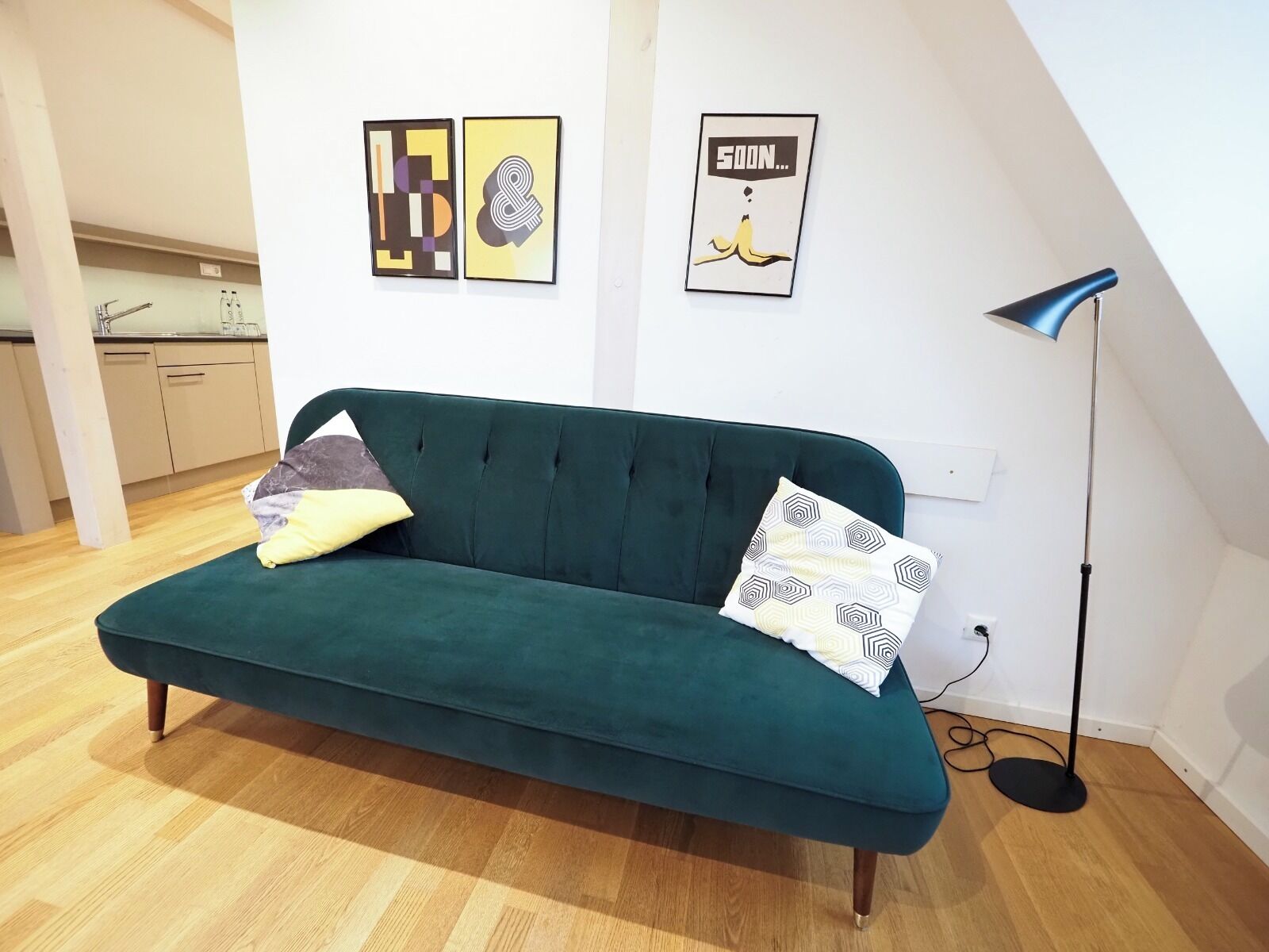 Um sofá verde com almofadas estampadas, uma luminária de chão e arte abstrata nas paredes em um espaço de estar moderno.