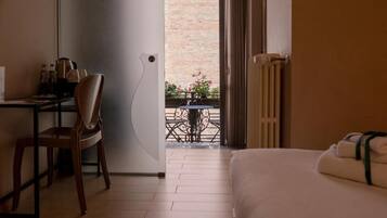 Quarto de hotel com cama, escrivaninha e cadeira, radiador e vista para uma varanda florida.