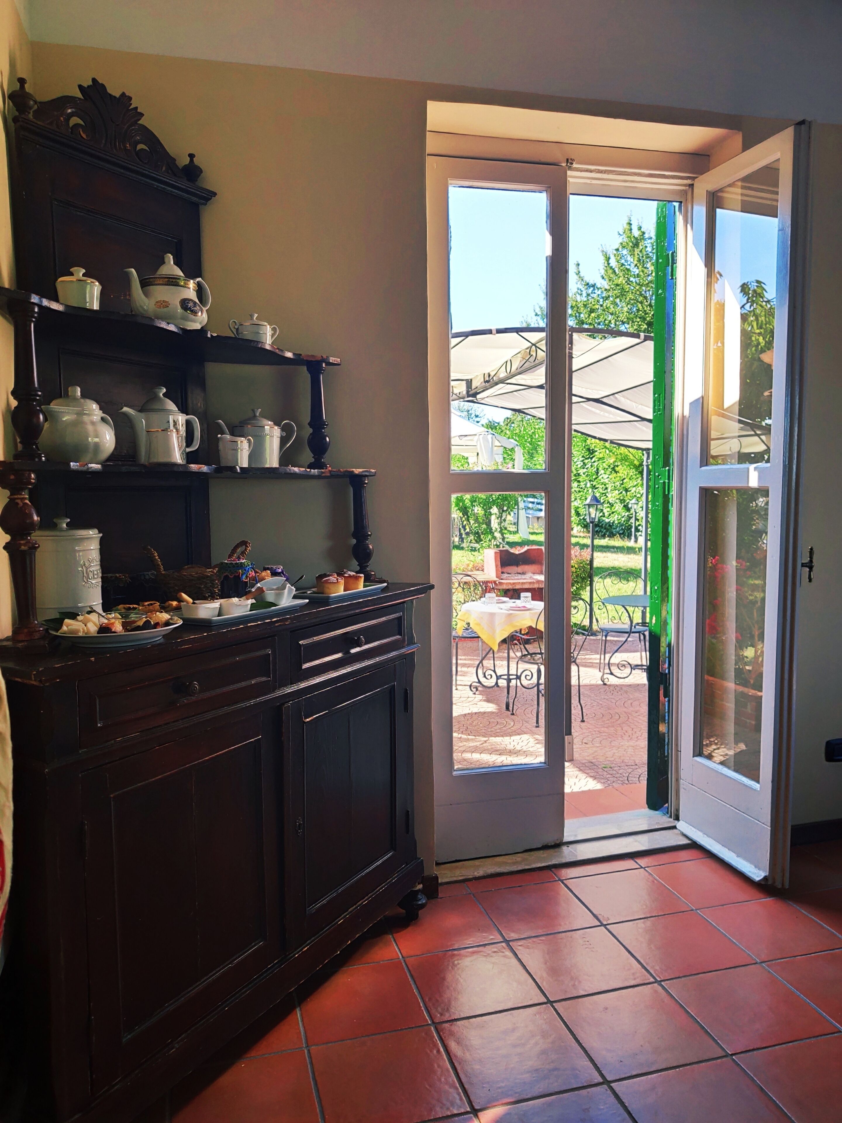 Cozinha com armários de madeira escura, bancada com bules e vista para um pátio externo através de uma porta de vidro.