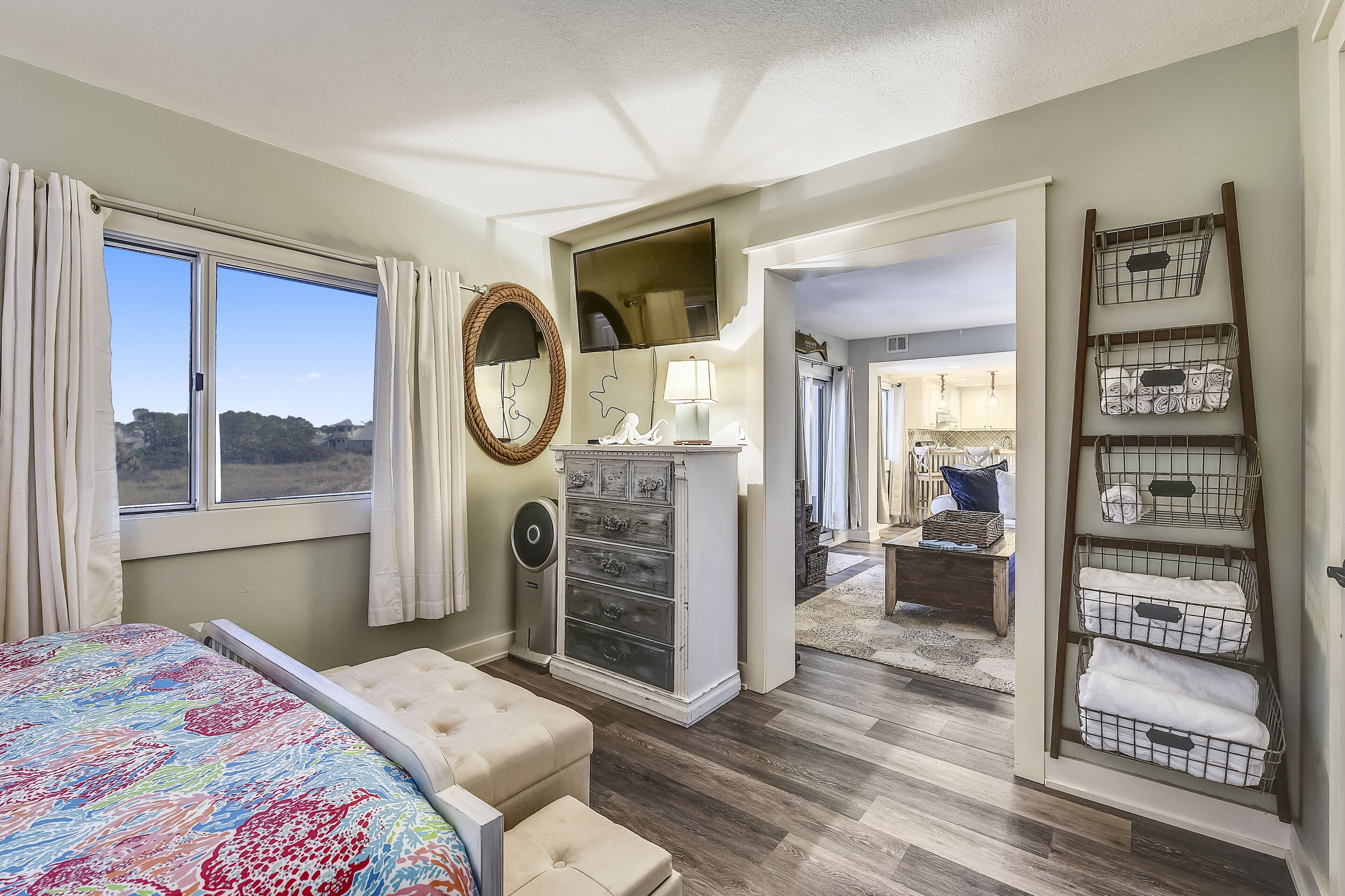 Quarto com uma cama grande, cômoda, espelho e vista para o exterior.