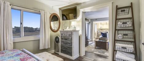 Quarto com uma cama grande, cômoda, espelho e vista para o exterior.