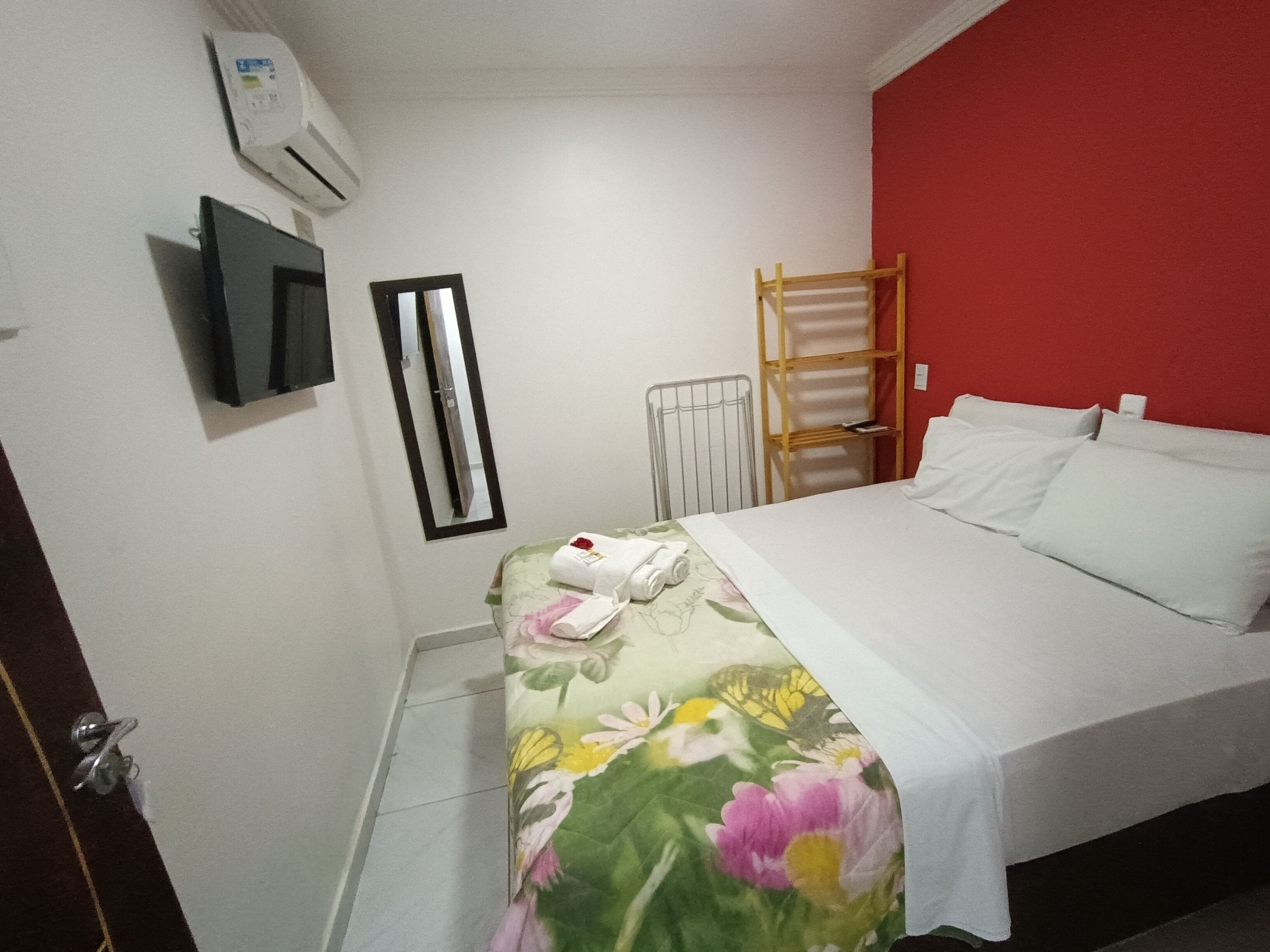 Quarto de hotel com uma cama, um espelho, um radiador e uma televisão na parede.