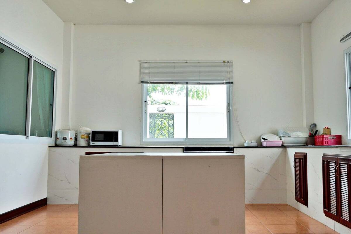 Cozinha com ilha central, micro-ondas, pia e janela com persianas.