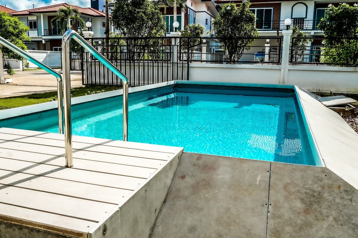 Piscina retangular com escada de metal e deck de concreto.
