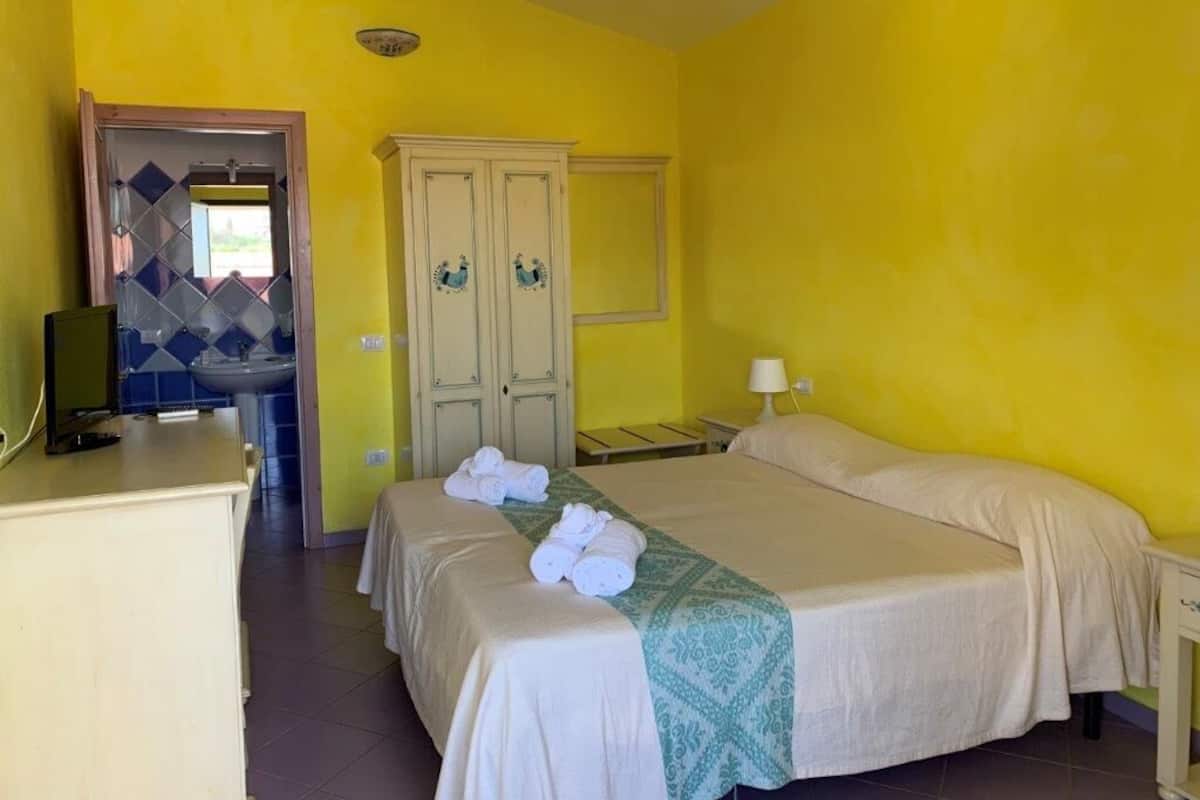 Quarto de hotel com duas camas, um guarda-roupa, uma pia e um espelho.