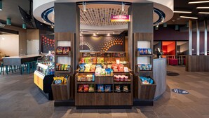 Quiosque de lanches com diversos produtos embalados e placa indicando serviço de comida e bebida 24 horas.
