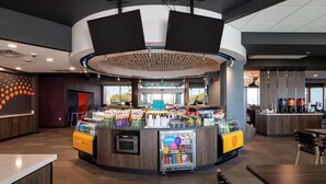 Uma praça de alimentação moderna com uma ilha central que inclui uma máquina de venda automática e um balcão refrigerado.