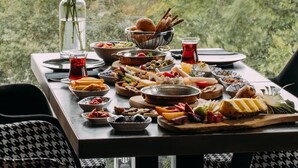 Mesa posta com diversos pratos e um vaso de flores, com vista para uma ponte e vegetação.