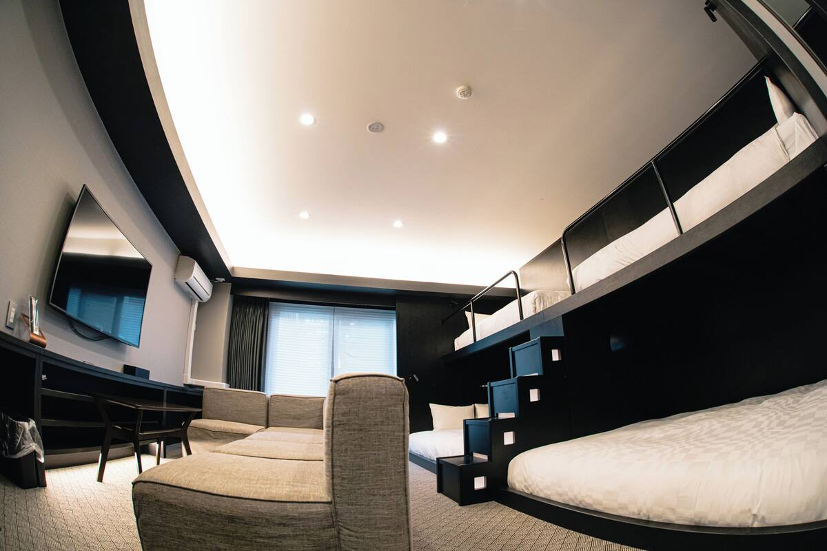 Quarto de hotel moderno com cama beliche, sofá, escrivaninha e televisão de tela plana.